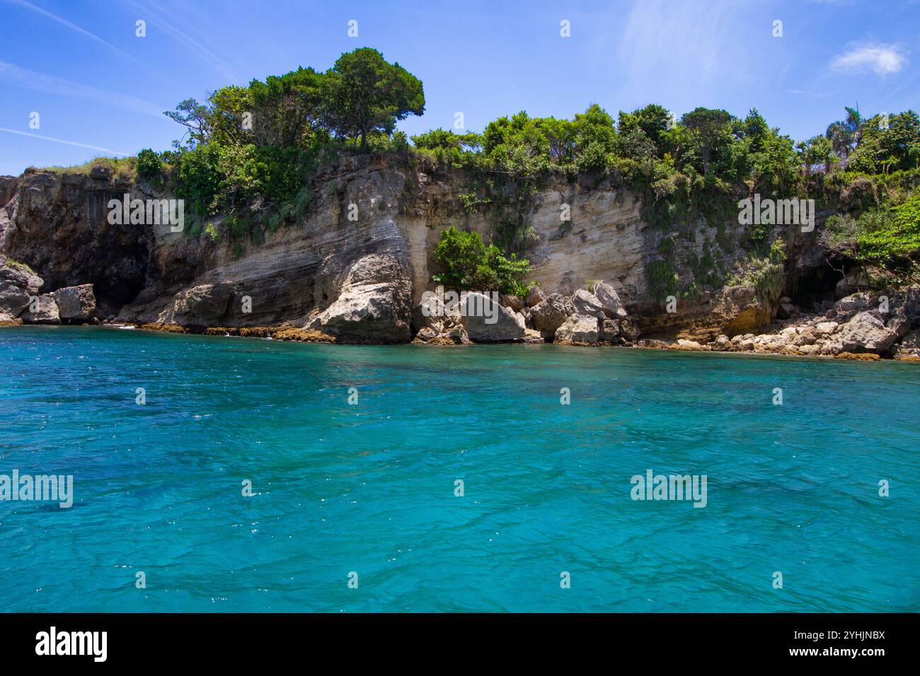 Gentle waves lap against rugged cliffs and a towering rock formation ...