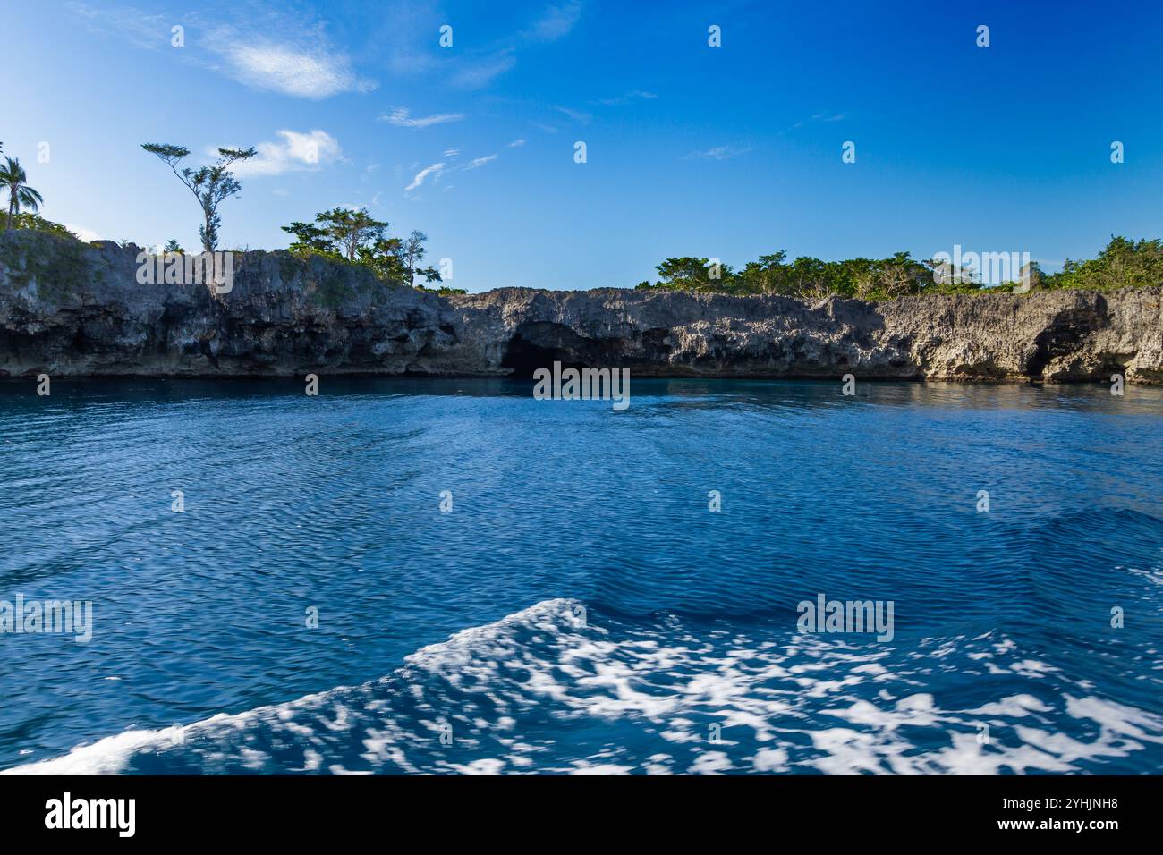 Gentle waves lap against rugged cliffs and a towering rock formation ...