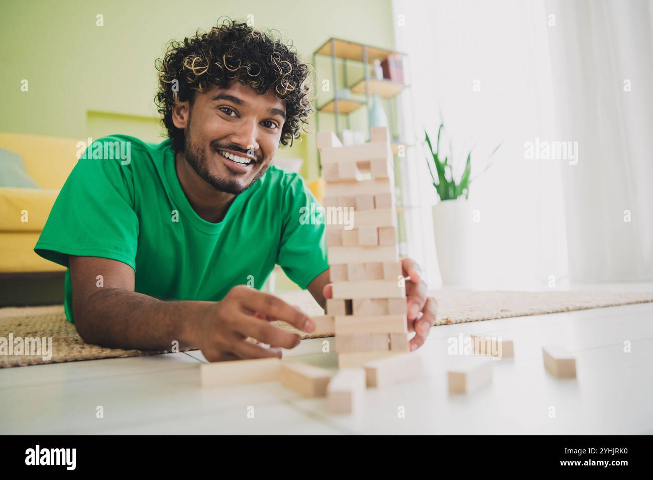 Photo of nice young man lay floor play jenga blocks wear t-shirt modern ...