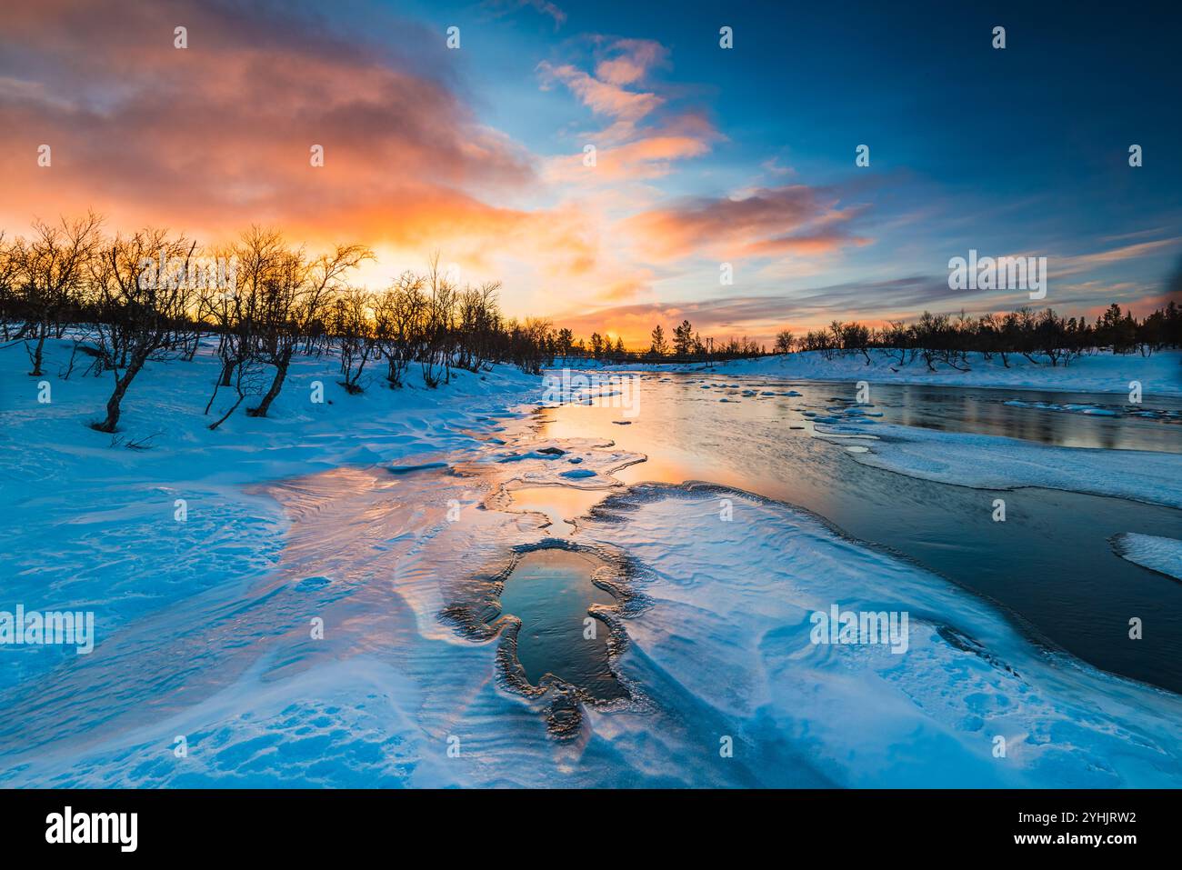 The vibrant sunrise casts a warm glow over a snowy river landscape ...