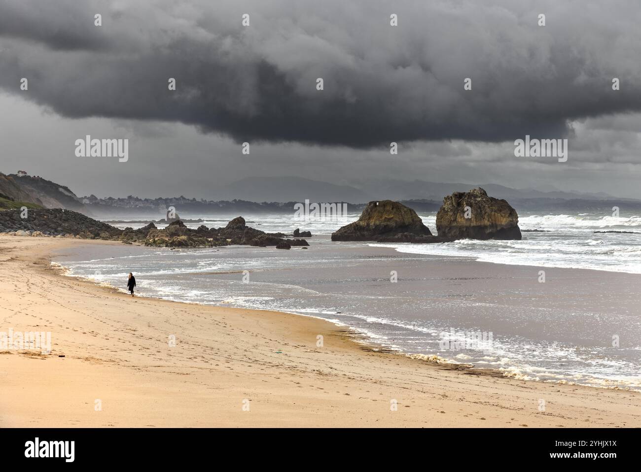 A lone person walking on the Plage de la Milady under a stormy sky ...