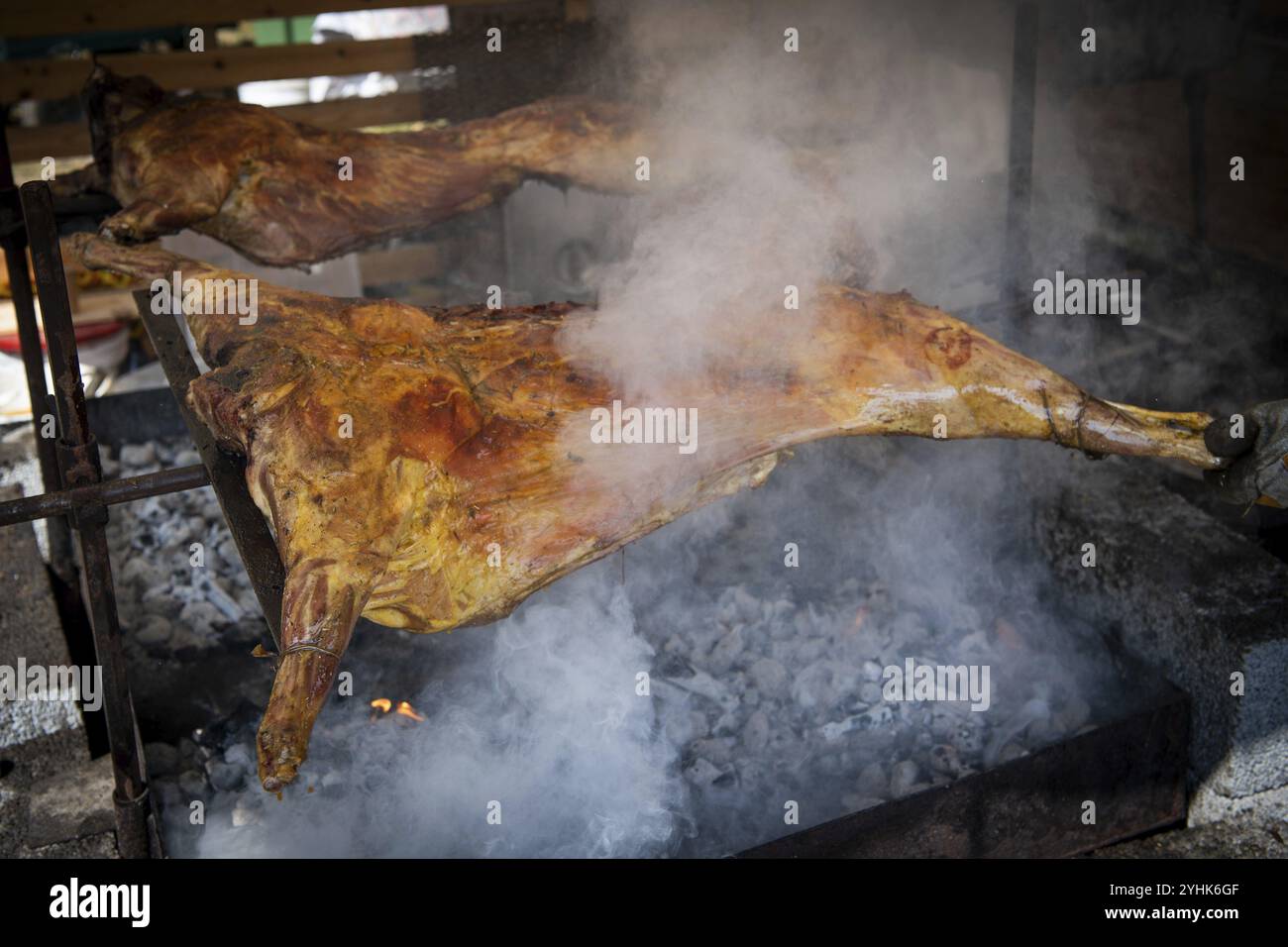 Traditionally grilled pork halves over charcoal, surrounded by smoke in ...