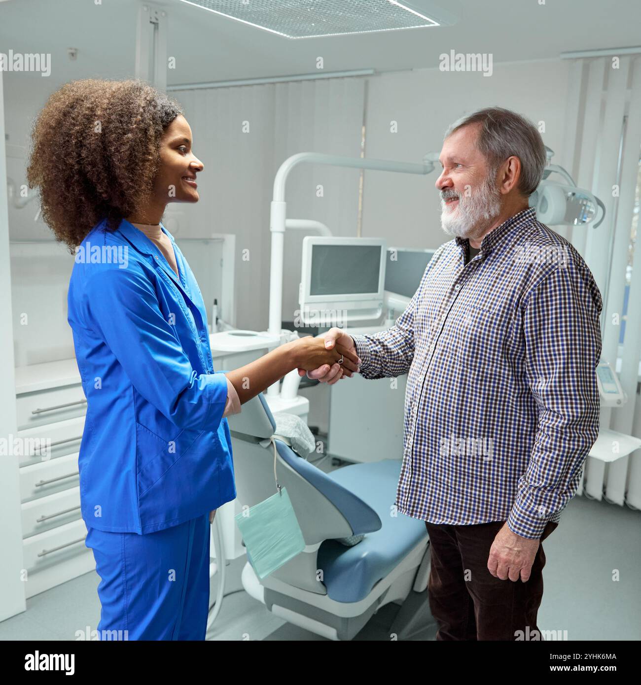 Dentist in blue scrubs warmly greets older patient with handshake ...