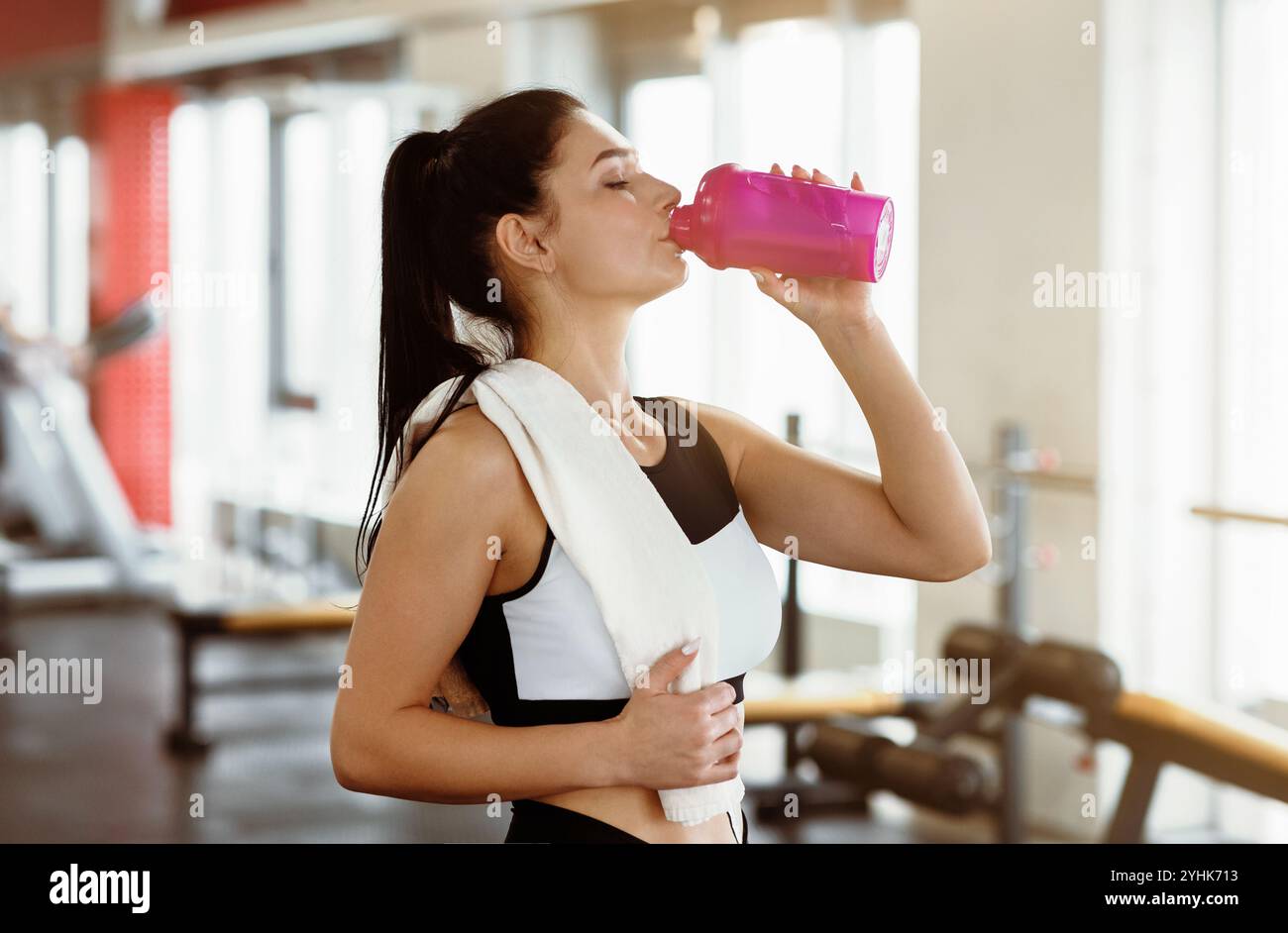 Keep hydrated. Young woman drinking water or protein cocktail in gym ...
