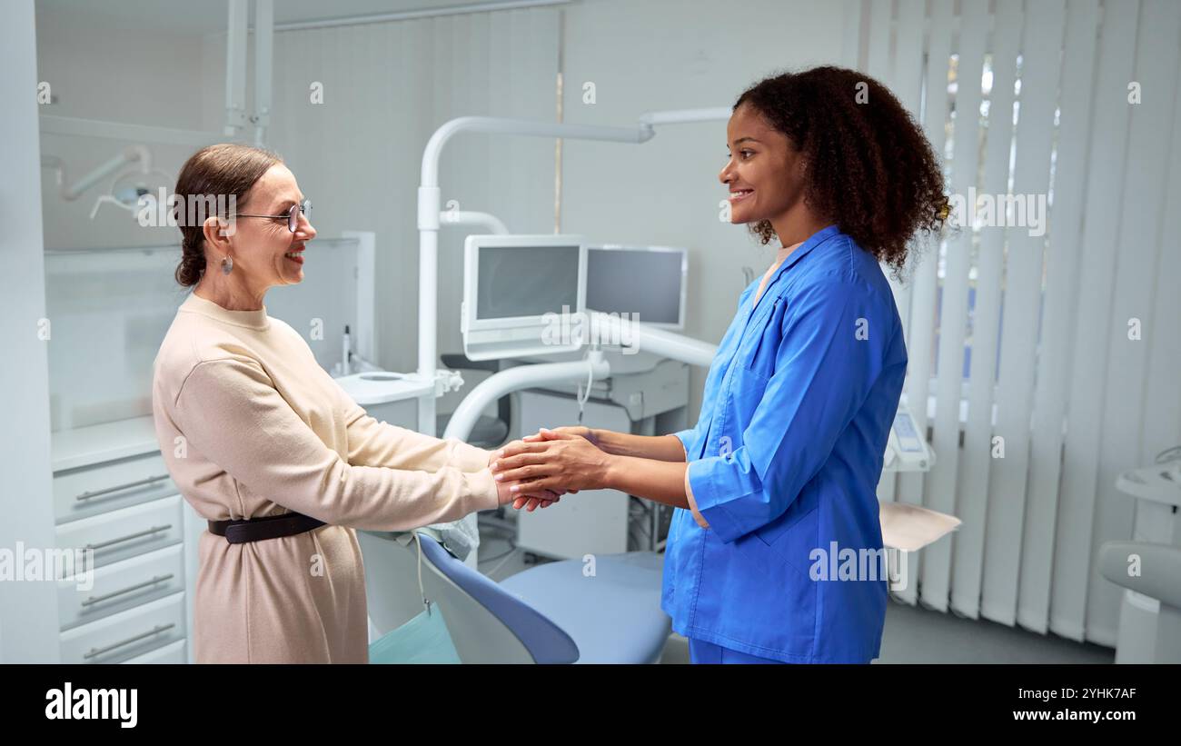 Dentist in blue scrubs warmly greets older patient with handshake ...