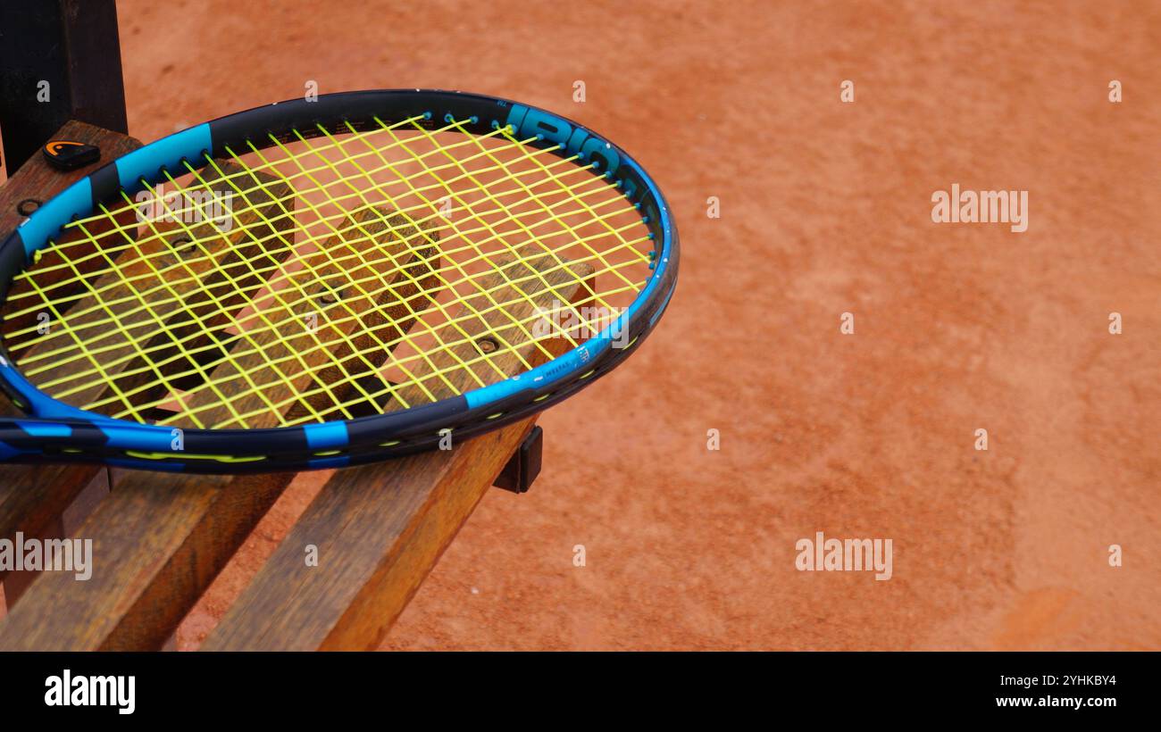 Tennis racket on bench in yellow and blue colors, clay court background ...