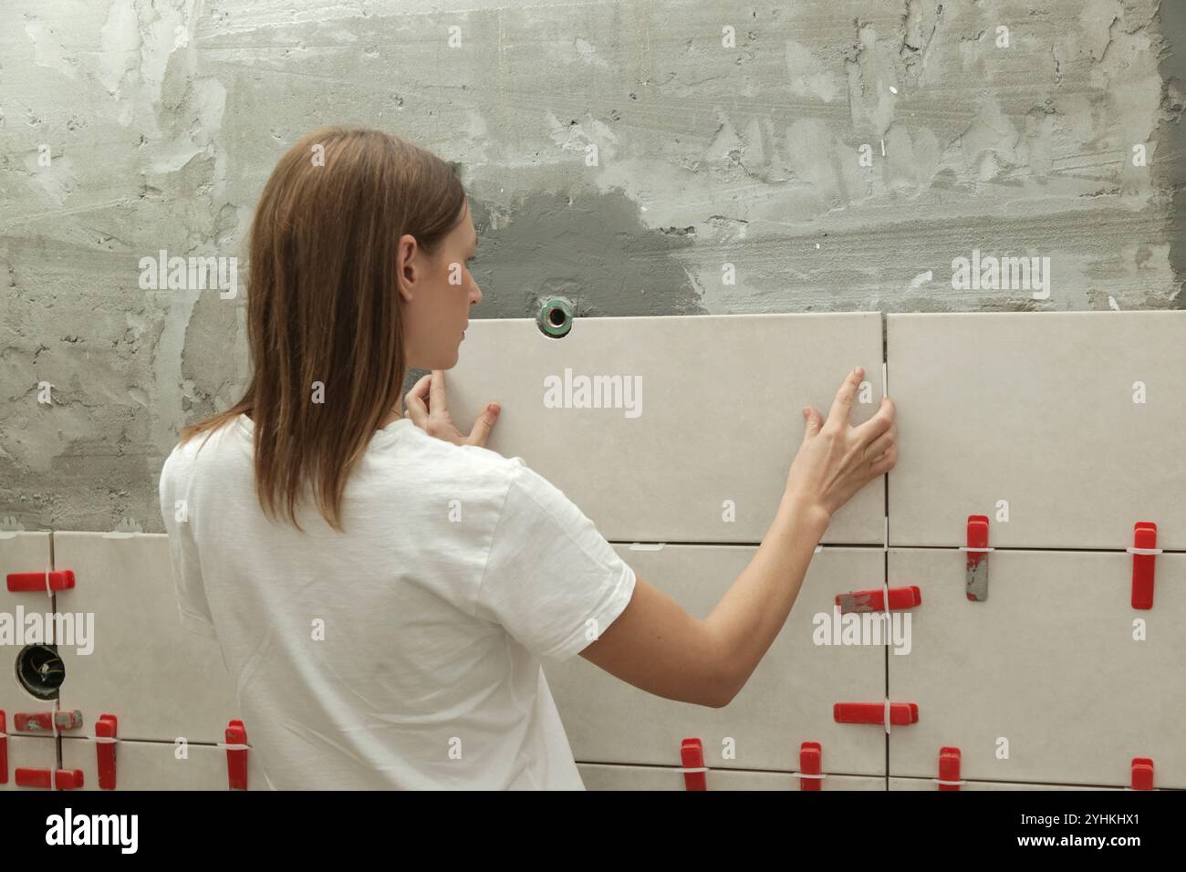 Woman tiling bathroom walls, applying adhesive on a tile and placing ...