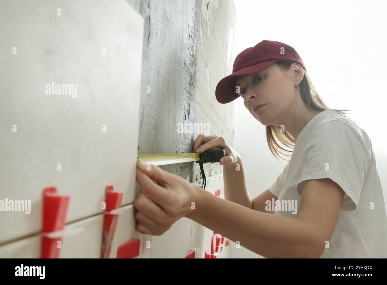 Woman tiling bathroom walls, using tape measure for measuring length ...