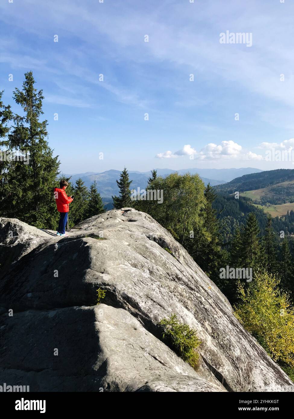 A lone individual in a red jacket stands on a rocky mountain ...