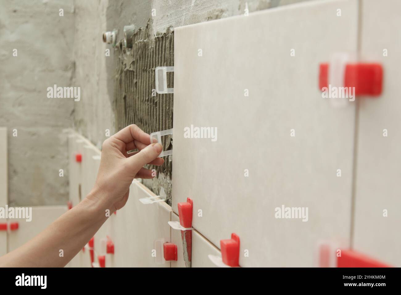 Woman tiling bathroom walls. Flat wall plastic tile leveling system ...