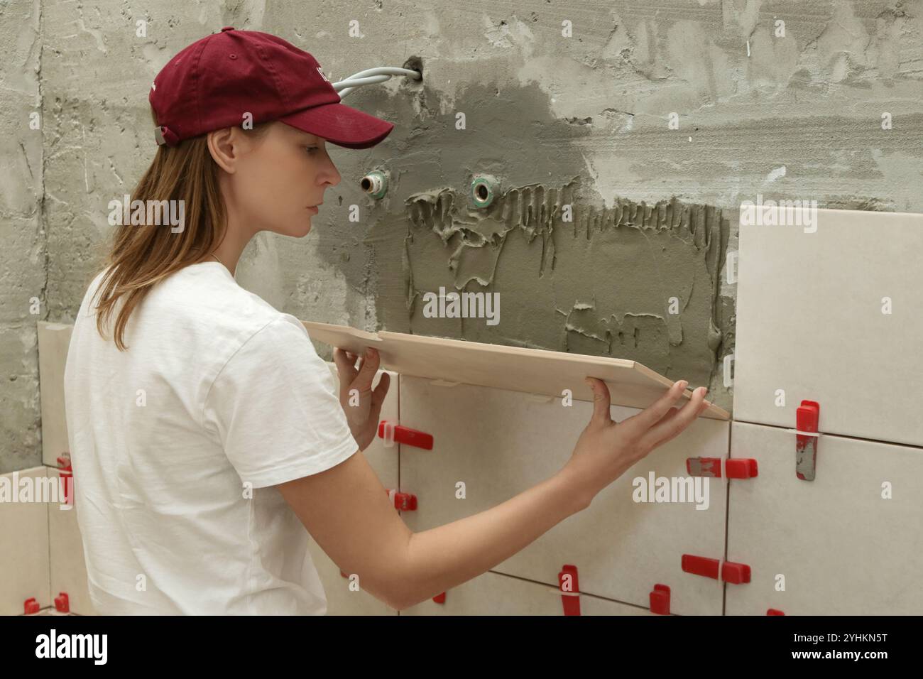 Woman tiling bathroom walls, applying adhesive on a tile and placing ...