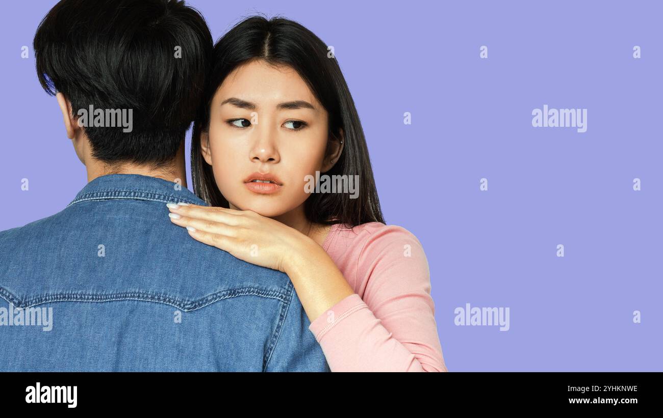 Scared asian girl hugging her boyfriend over grey background Stock ...