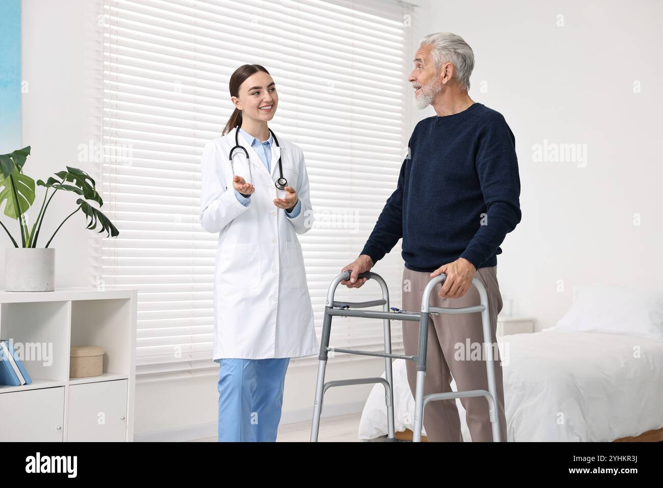 Doctor consulting senior patient with walking frame in hospital ward ...