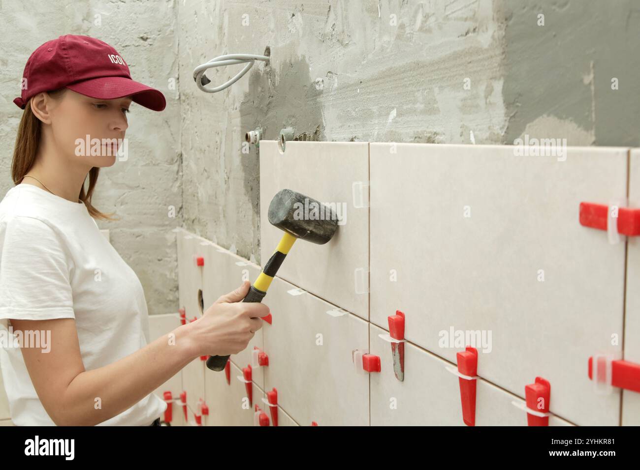 Woman tiling bathroom walls, pressing tile into a glue with rubber ...