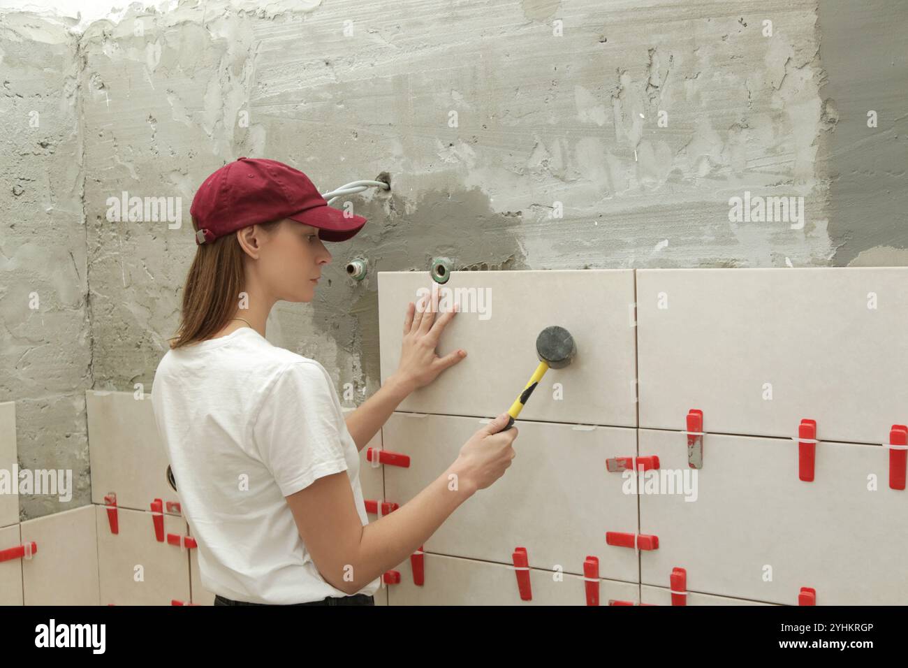 Woman tiling bathroom walls, pressing tile into a glue with rubber ...