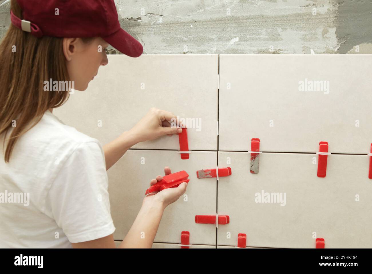 Woman tiling bathroom walls. Flat wall plastic tile leveling system ...