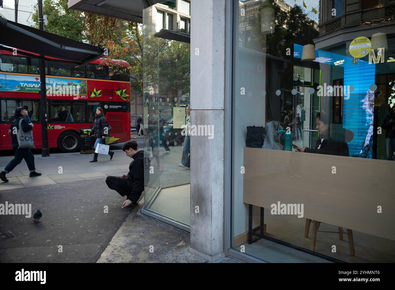 A high street worker takes a cigarette break whilst crouched down along ...