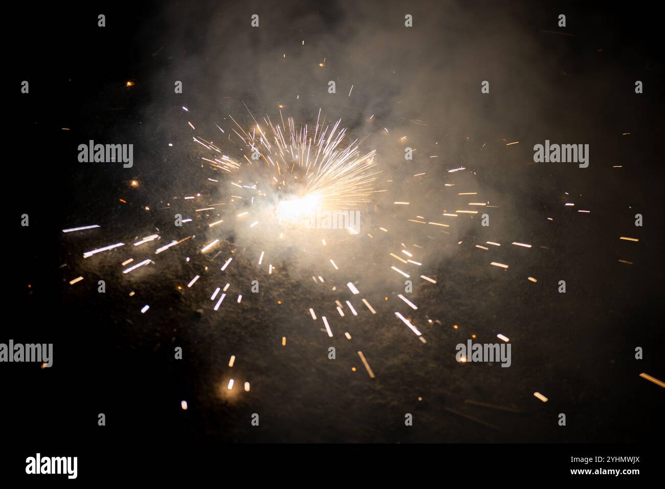 Bright sparks burst from a firework on the ground, radiating light and ...