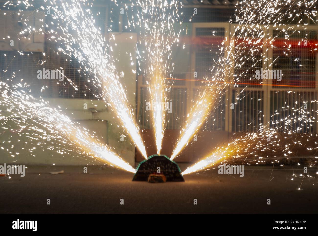 Ground-level firework fountain sprays sparks, illuminating a city night ...