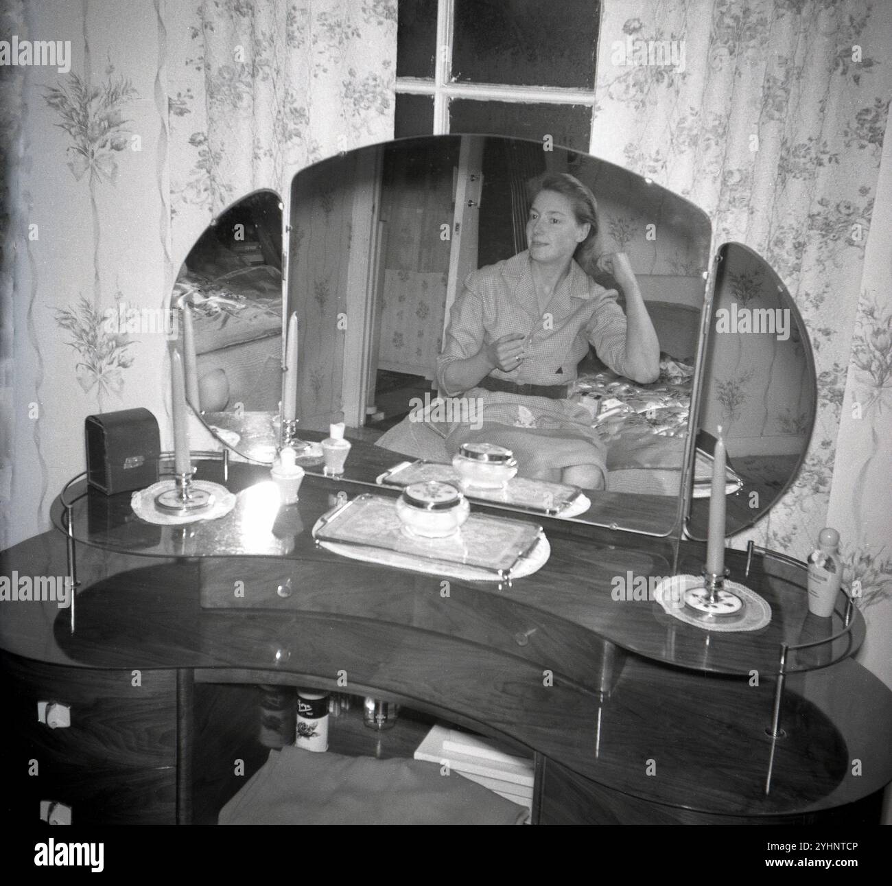 1960s, historical, inside a bedroom, a lady on sitting on a bed, brushing her hair, her ...