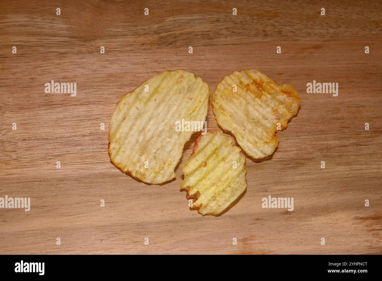 Three unique potato chips are placed on a wooden table, exhibiting a ...
