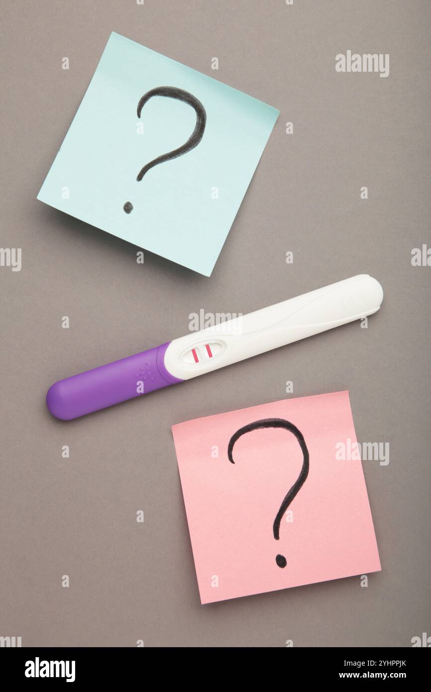 Pregnancy test with two stripes with question marks on grey background ...