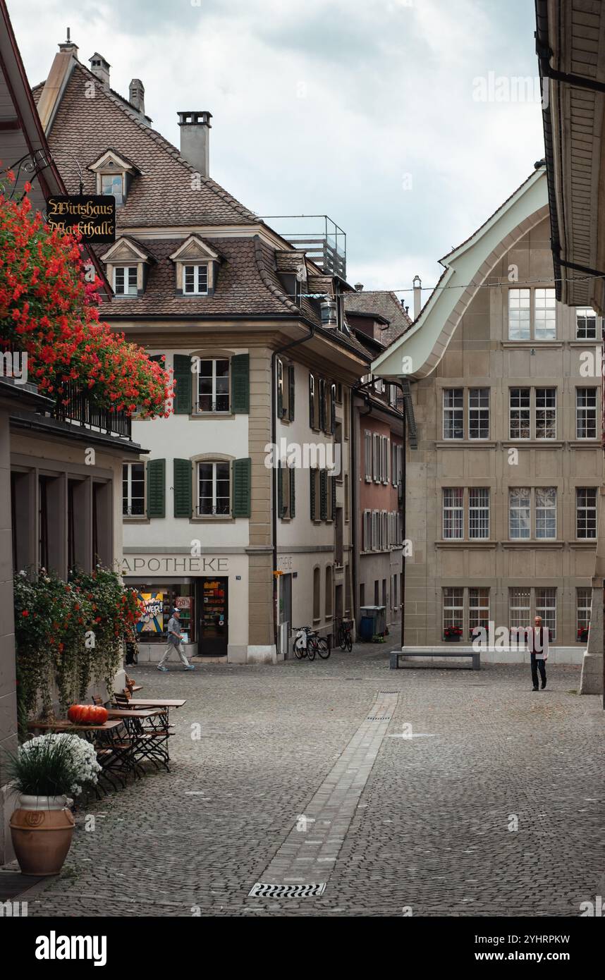 Square in a Swiss town with old buildings. Cafe tables and flower pots ...
