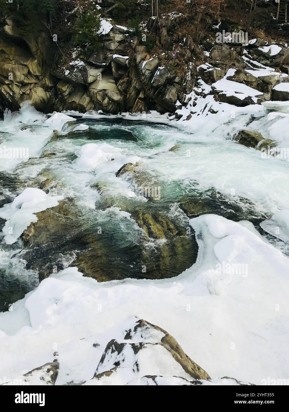 A beautiful winter waterfall cascades among snow-covered rocks ...