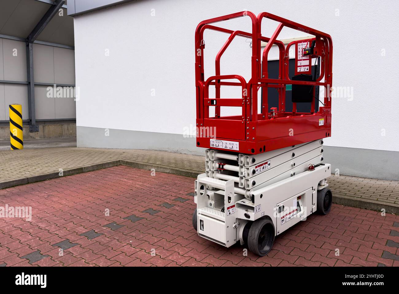A red and white elevated platform lift stands idle on a brick pathway ...
