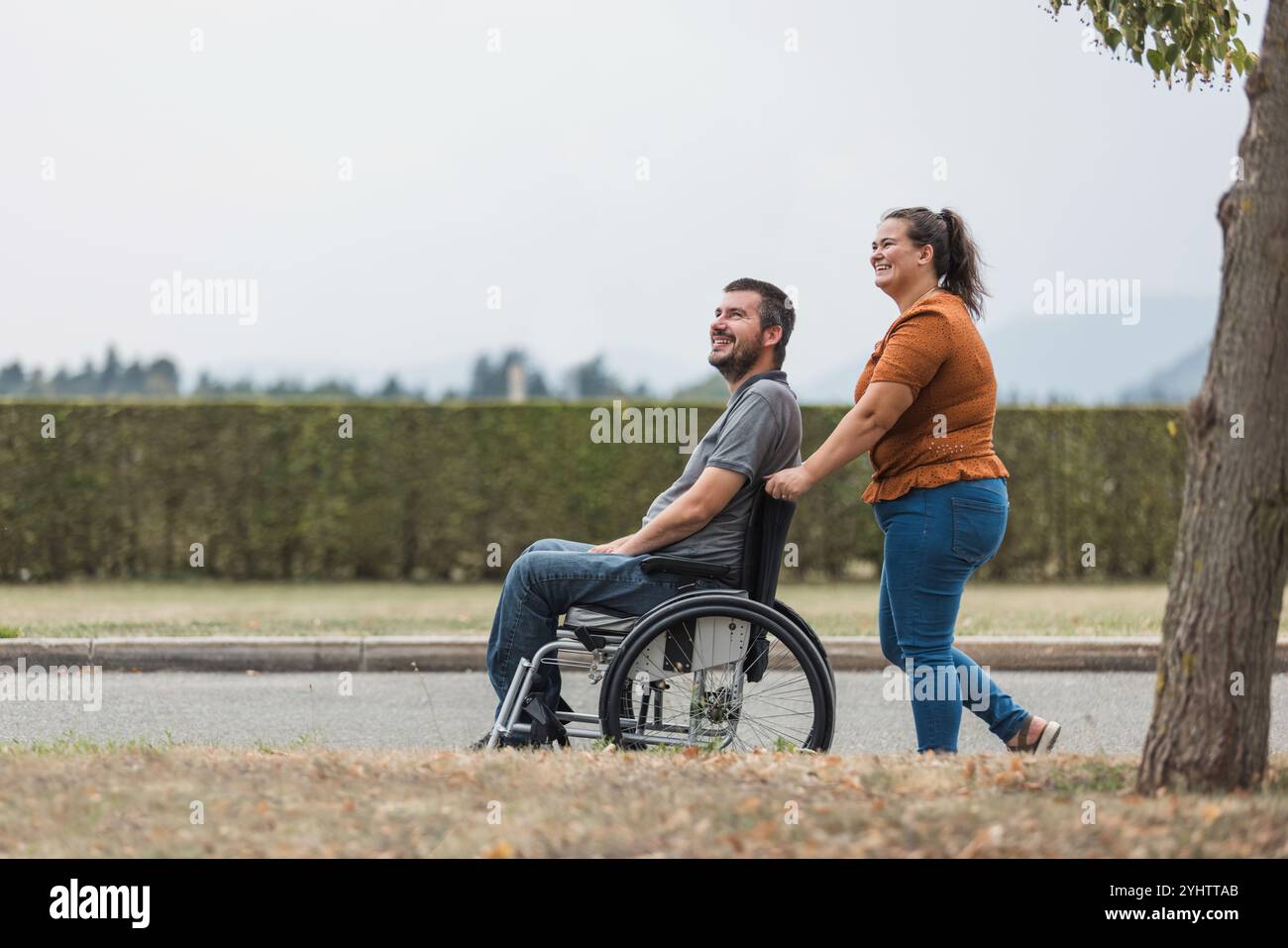 Smiling man, a wheelchair user, and his female assistant enjoying ...
