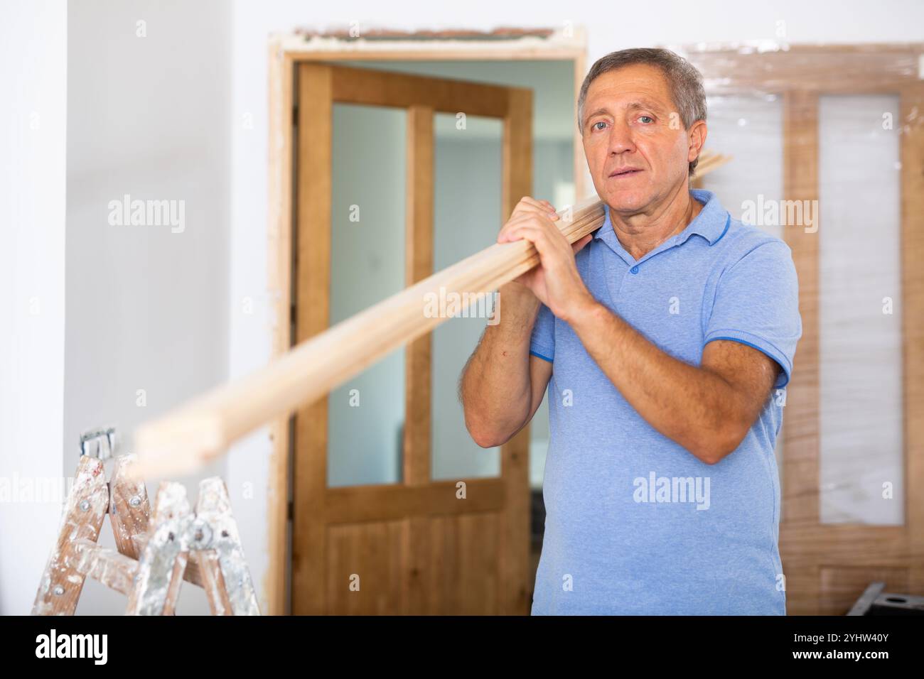 Middle-aged male carpenter in uniform holding wooden planks indoors ...