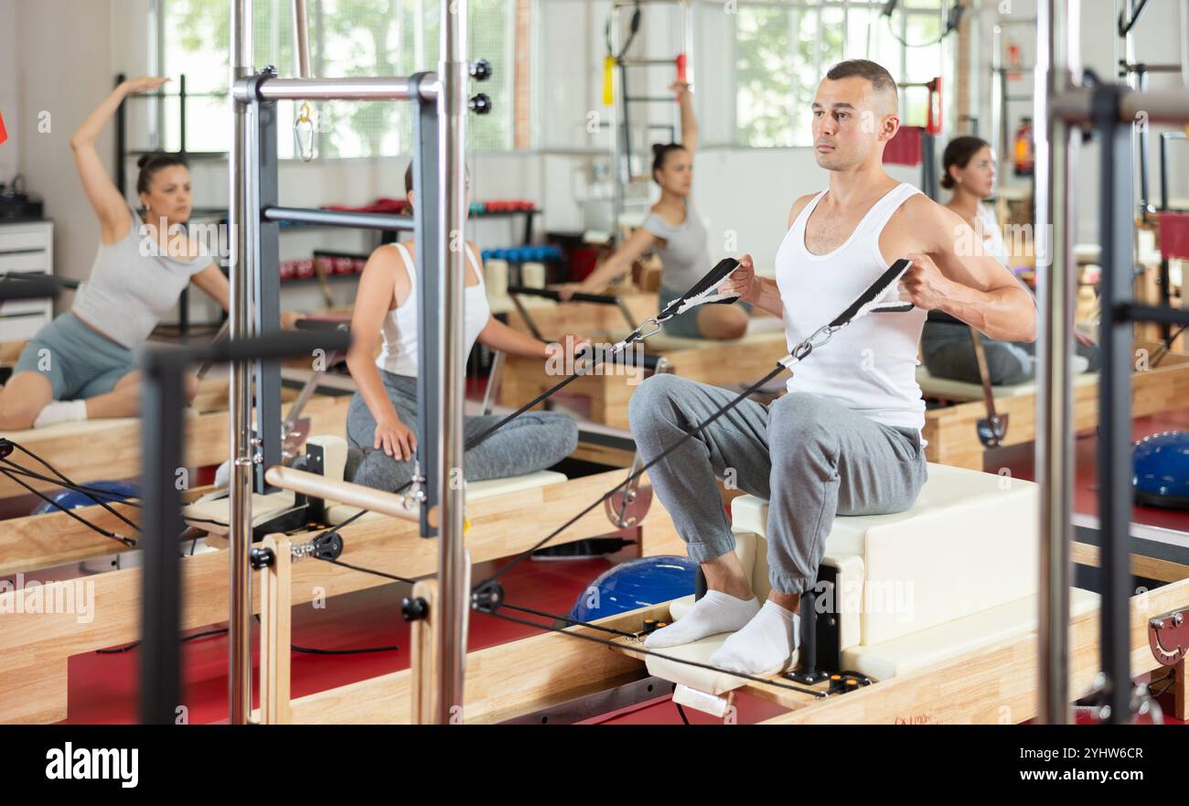 Young guy doing arm exercises on cable reformer device Stock Photo - Alamy