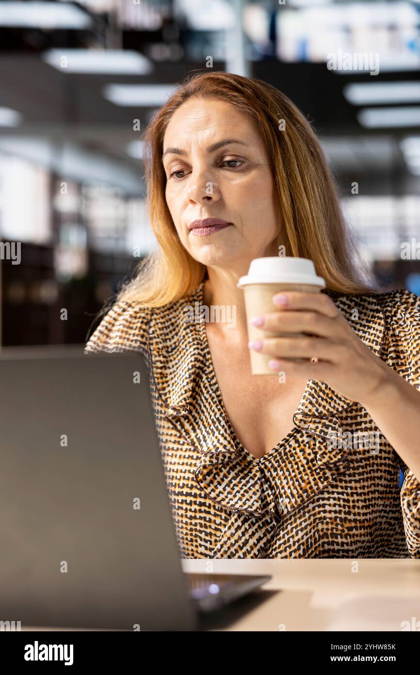Adult entrepreneur drinking cup of coffee and multitasking at her ...