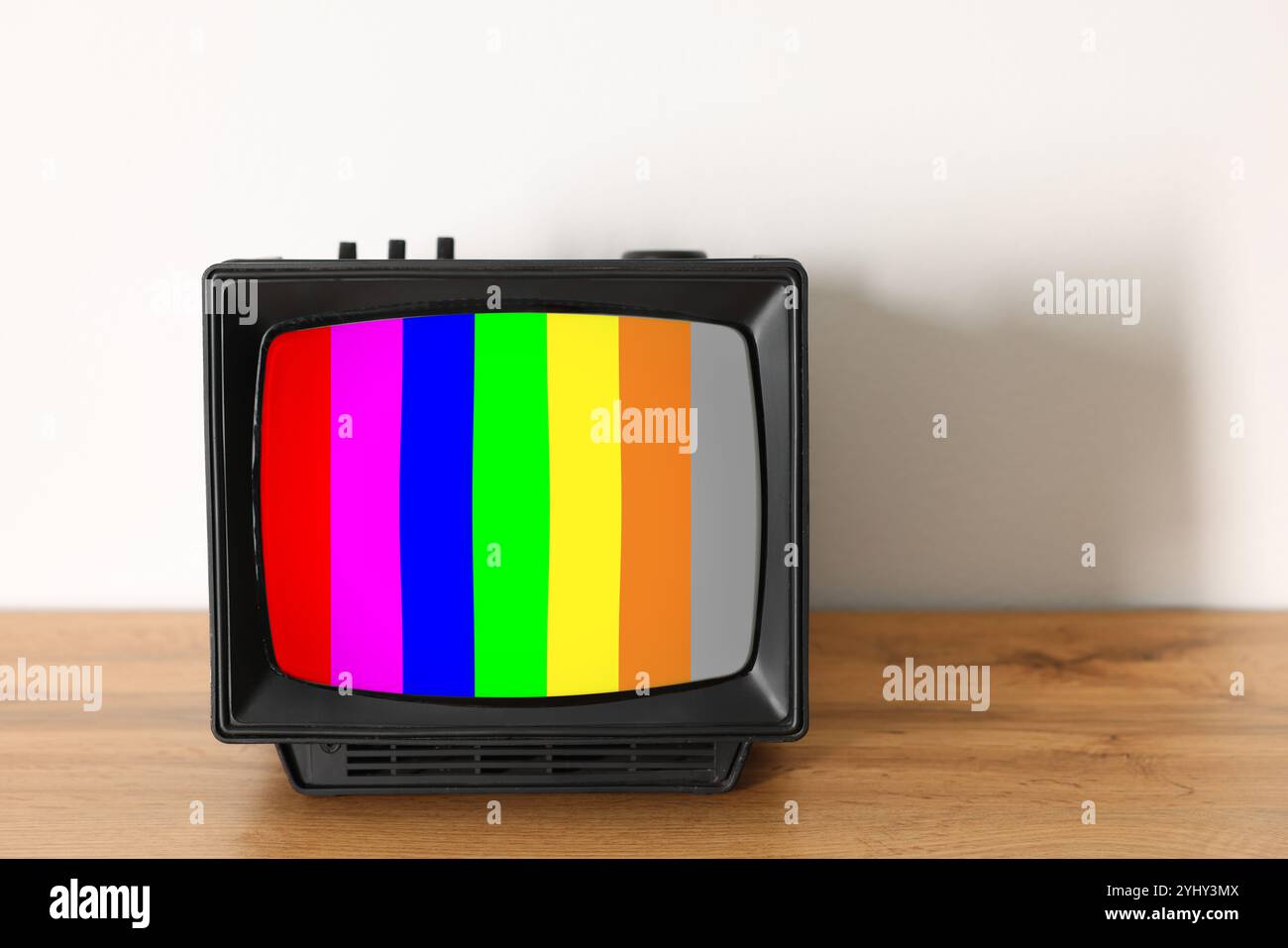 Retro TV set with test pattern on wooden table near white wall. Color ...