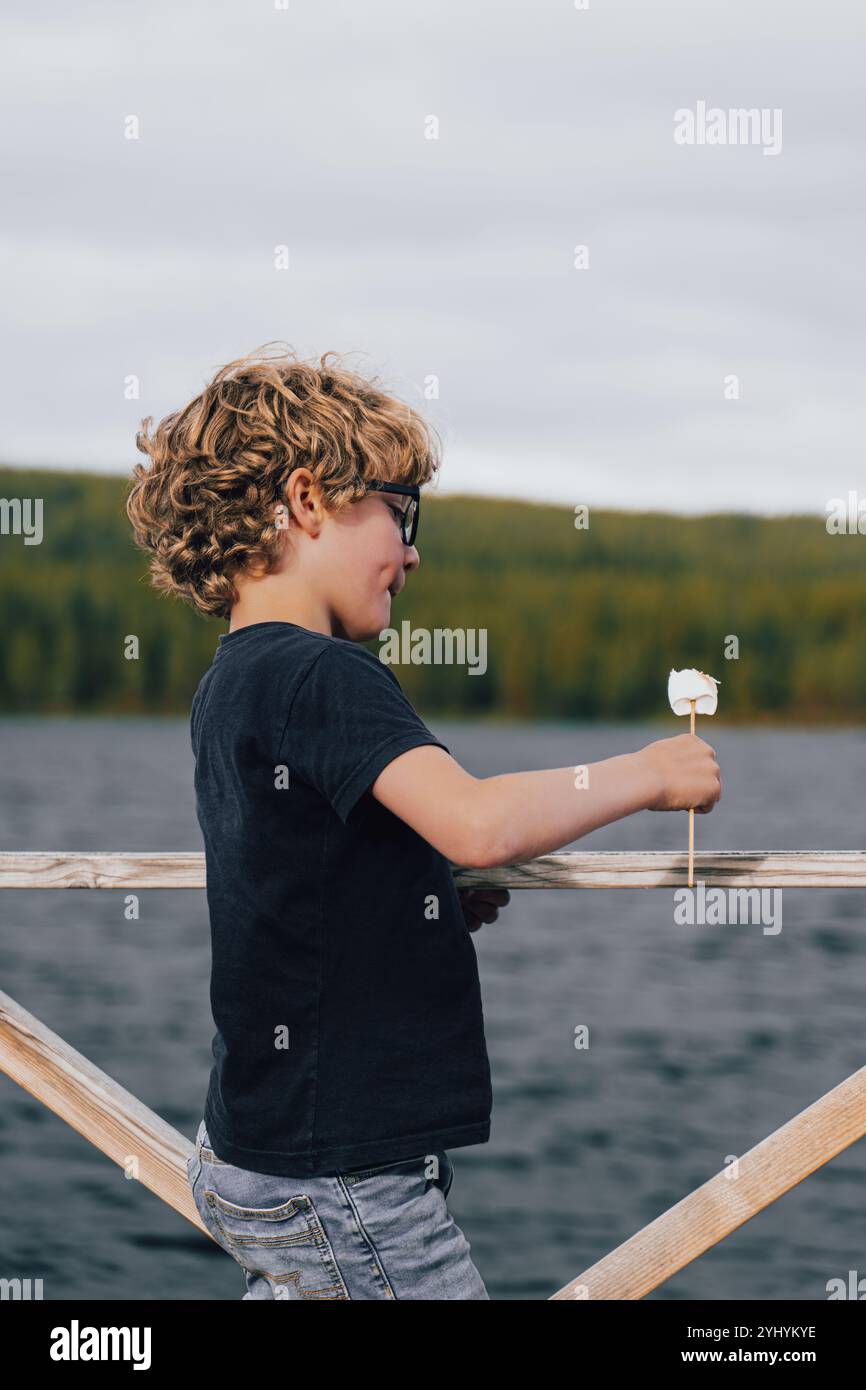 Cute young boy with blond curly hair enjoying a roasted marshmallow on ...