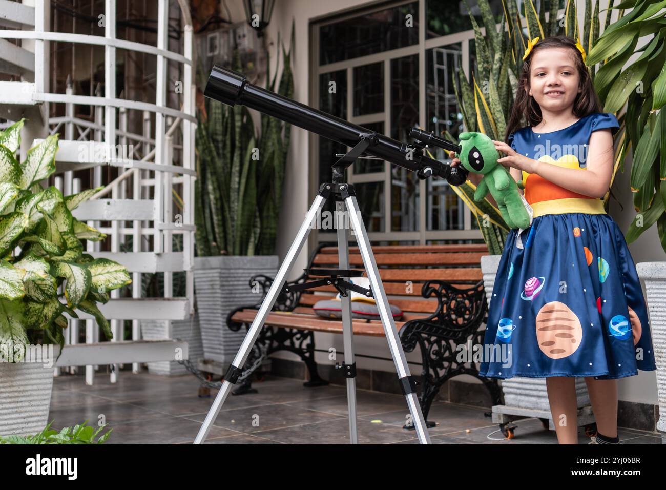 Young girl with an alien plush beside a telescope, wearing a space ...