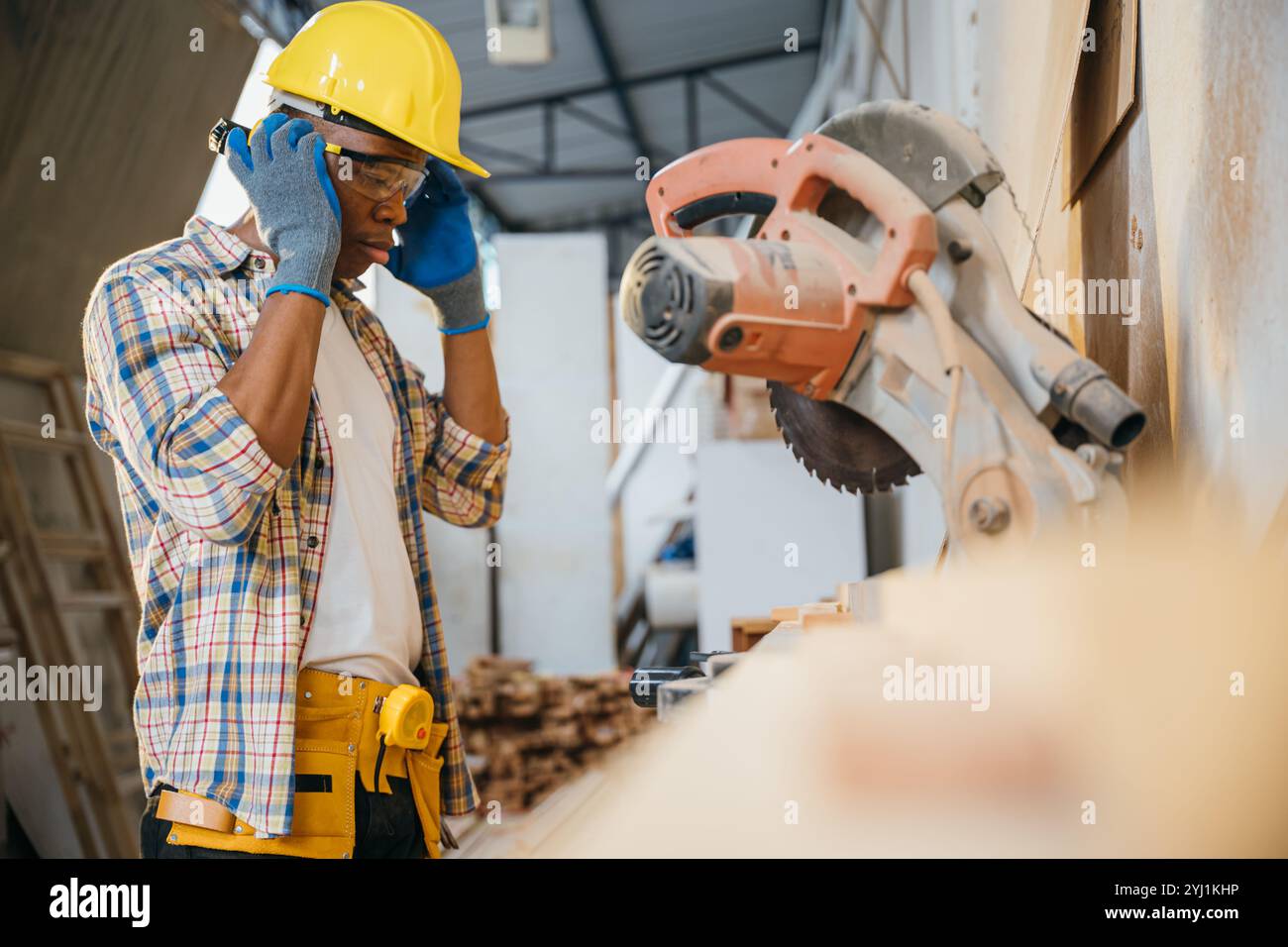 Construction worker in a yellow helmet using a chop saw to cut wood ...