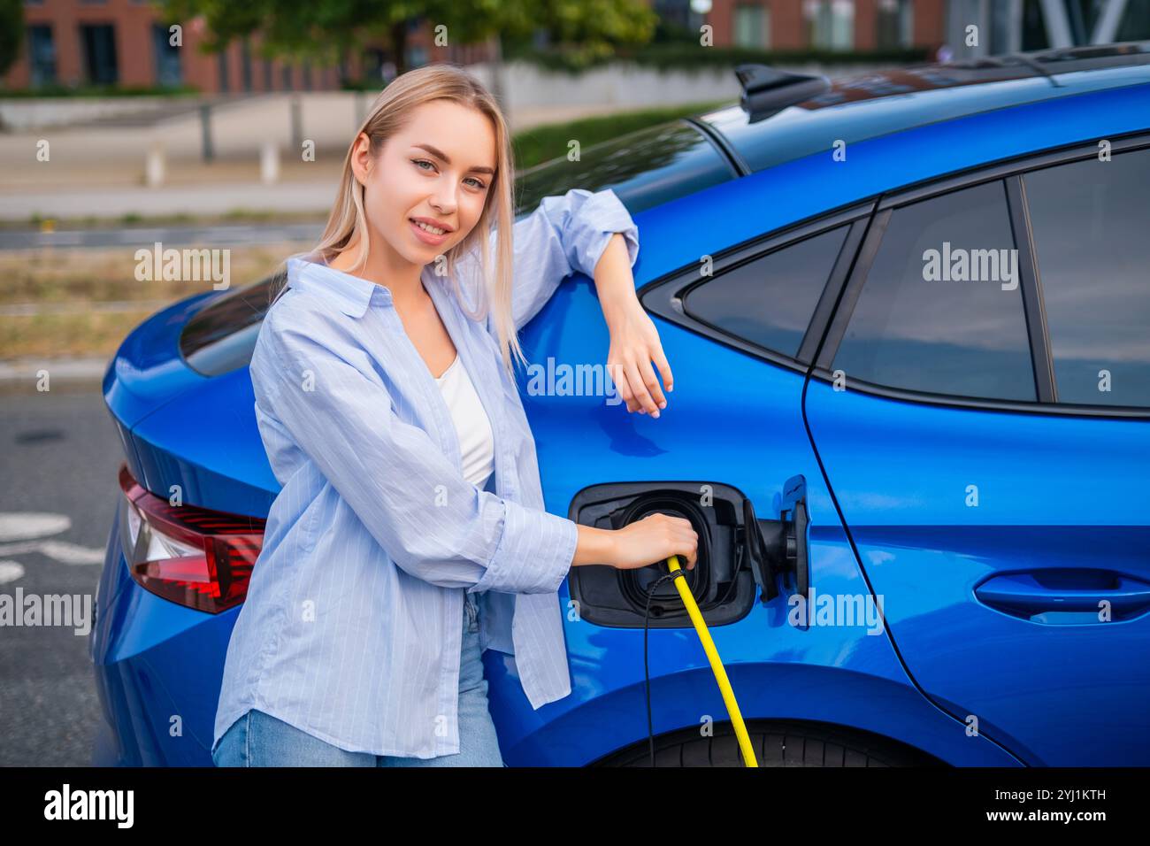 Portrait of blonde woman in casual clothes charging her electric car at ...