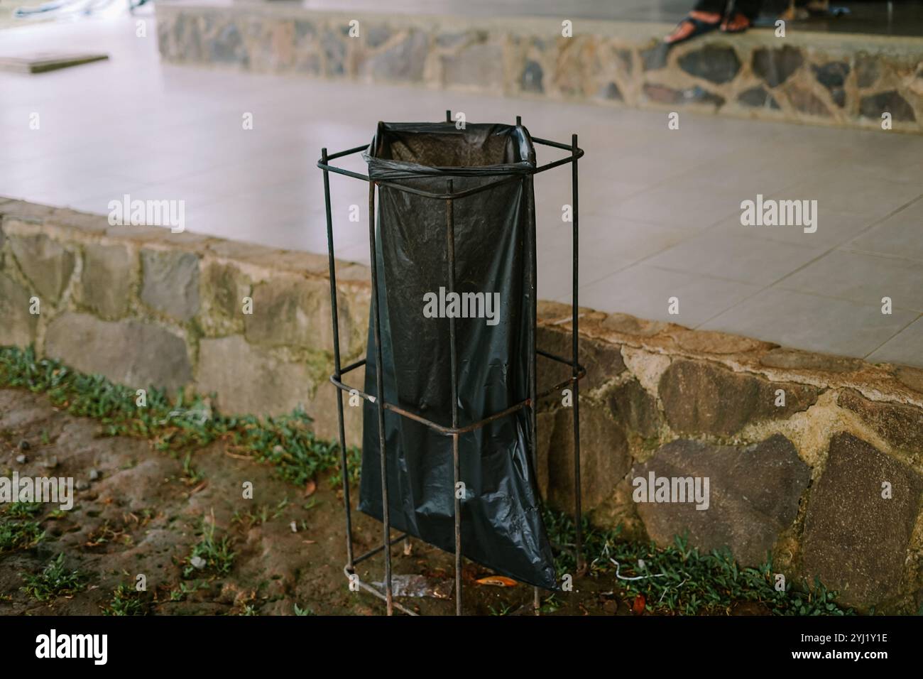 An outdoor trash bin with a black plastic liner, set against a natural ...