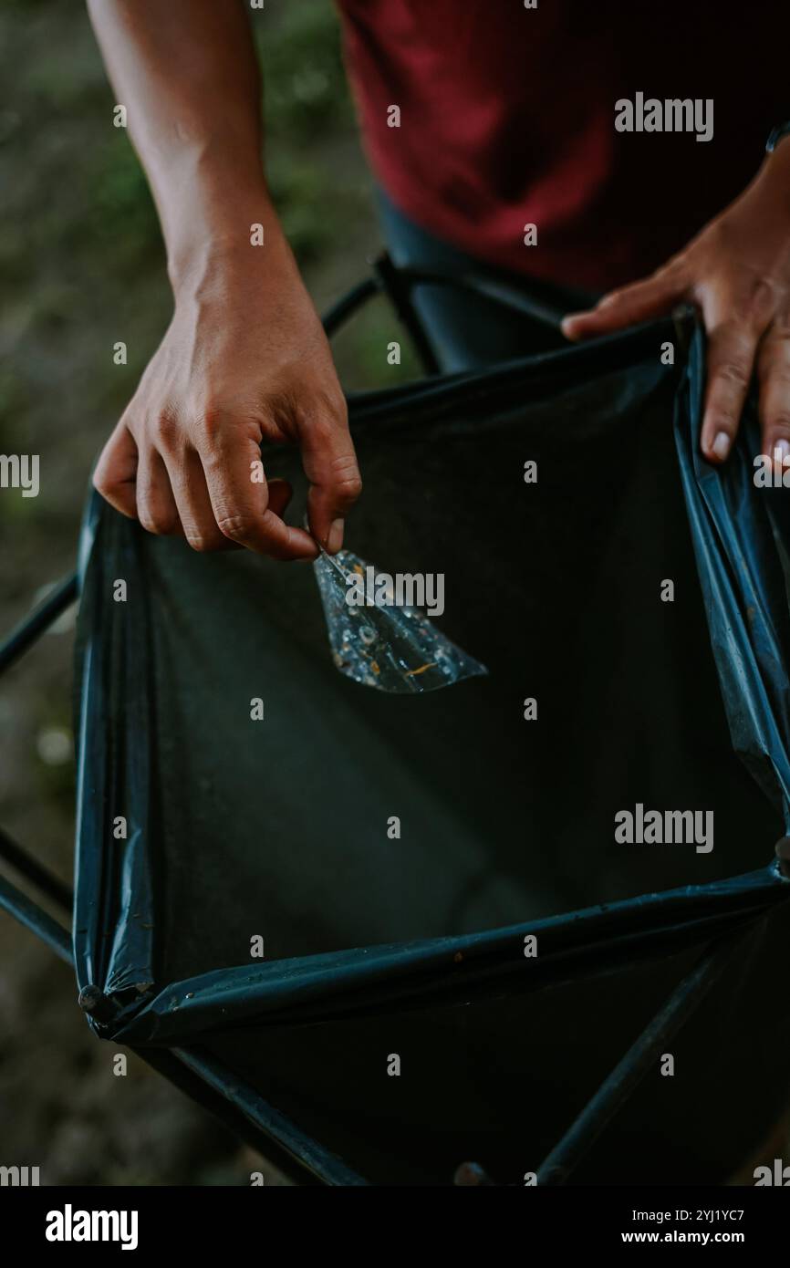 An outdoor trash bin with a black plastic liner, set against a natural ...