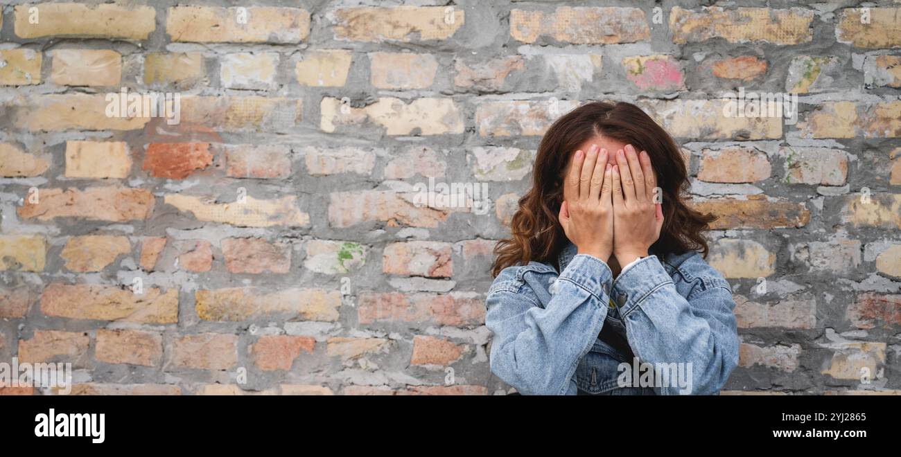 Upset girl sitting with face covered by hands near brick wall on street ...