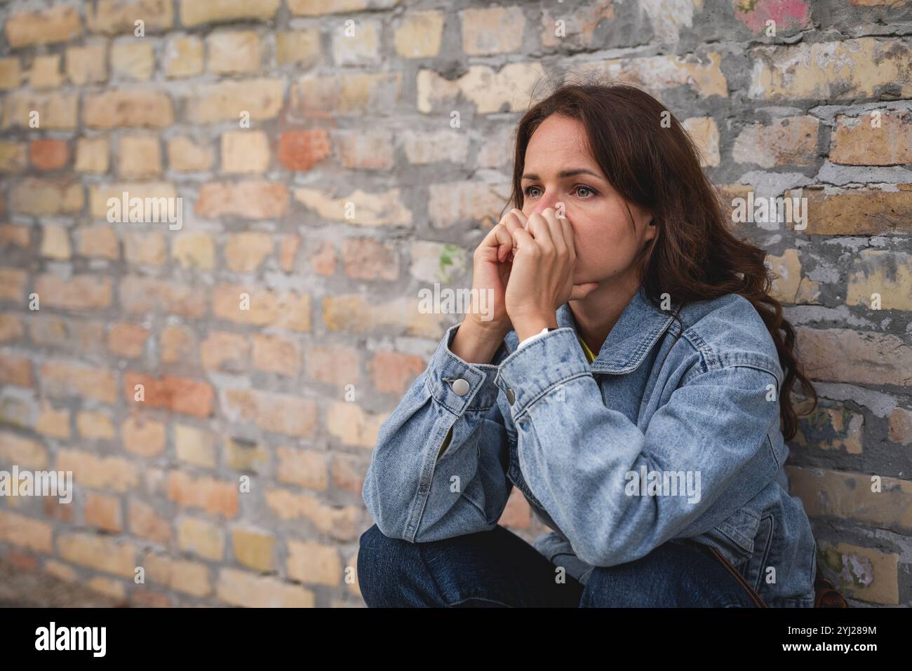 Frustrated Caucasian woman sits next to brick wall Stock Photo - Alamy