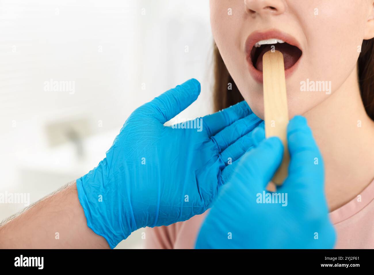 Doctor examining woman's throat with tongue depressor in clinic ...