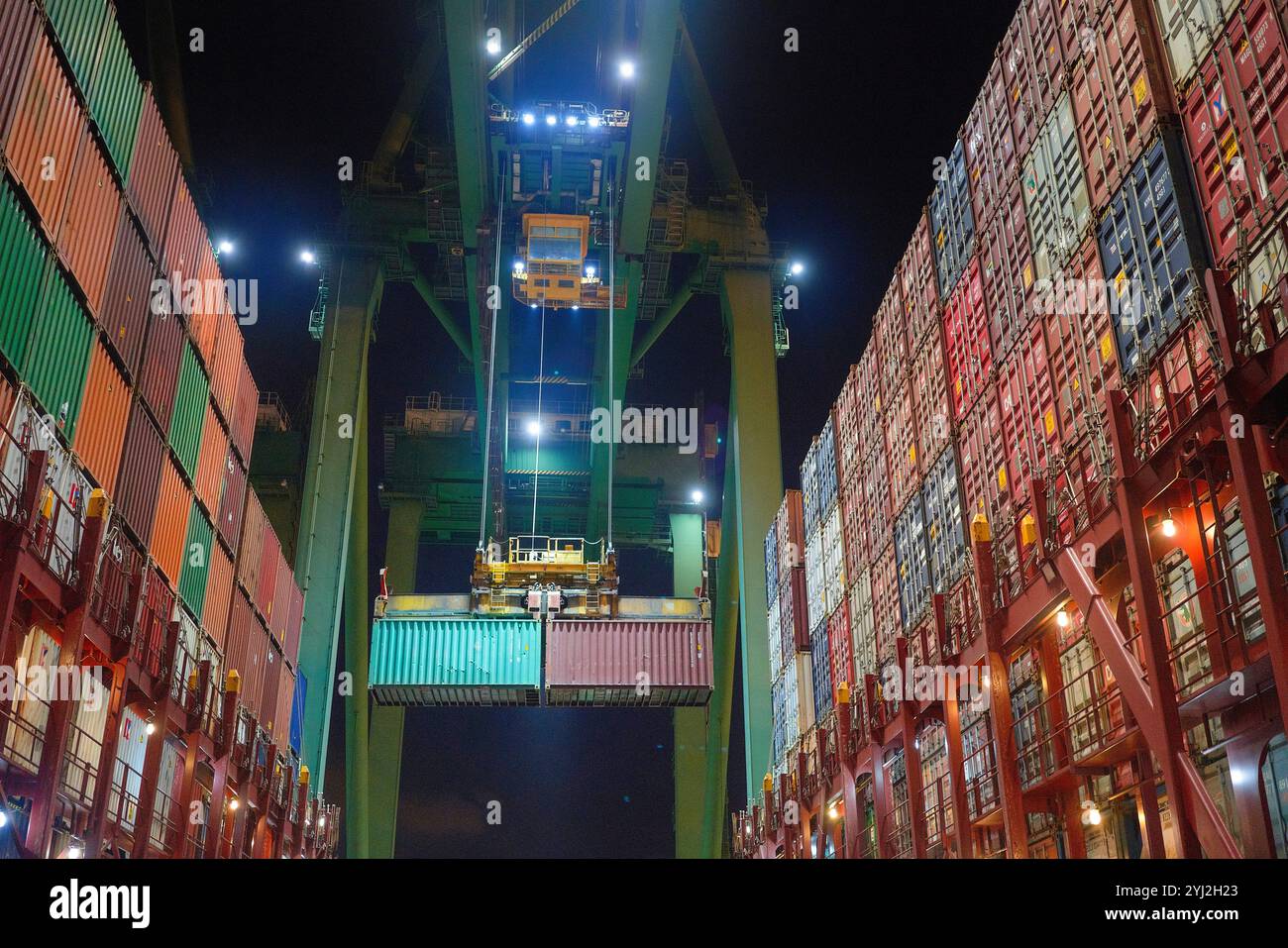 Nighttime view of a cargo ship being loaded with colorful shipping ...
