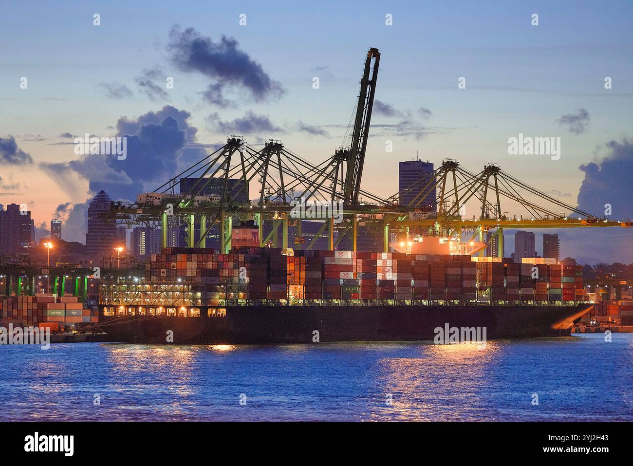 Container ship at port during twilight, with cranes and city skyline in ...