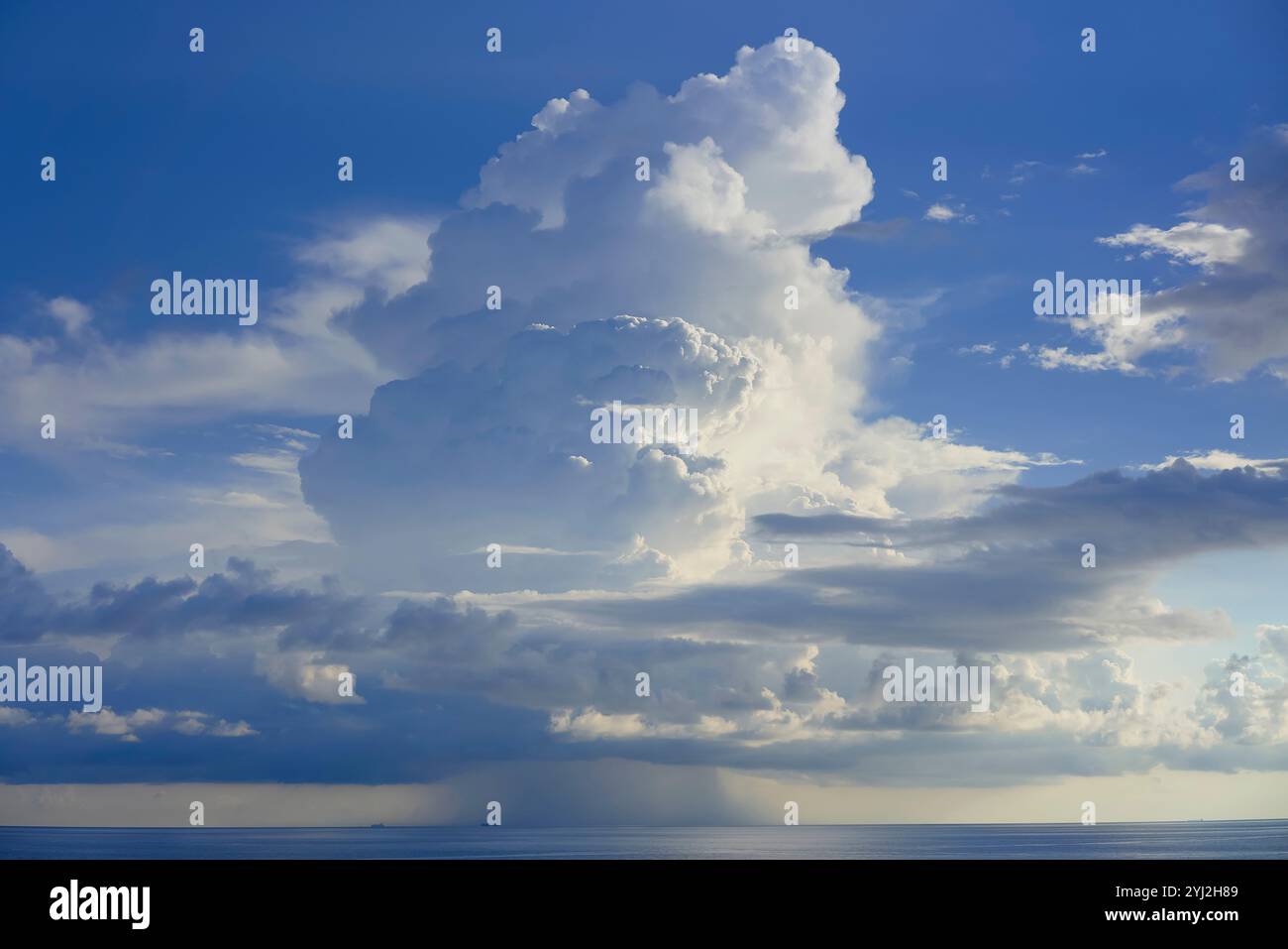 Majestic cumulus cloud towering over a serene sea under a blue sky with soft light piercing ...
