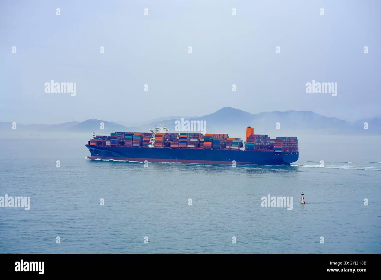 Cargo ship loaded containers sails through misty mountains faintly ...