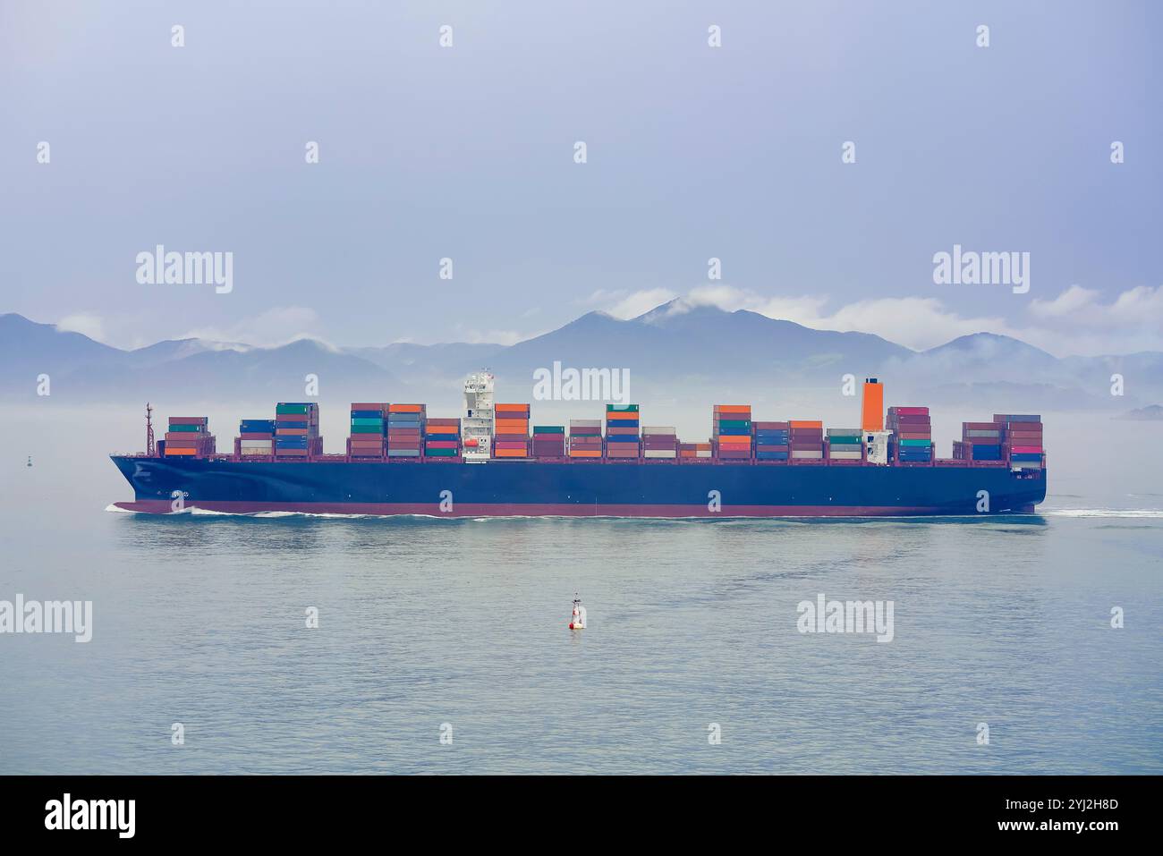 Cargo ship sailing on a foggy ocean with a tranquil mountain backdrop ...
