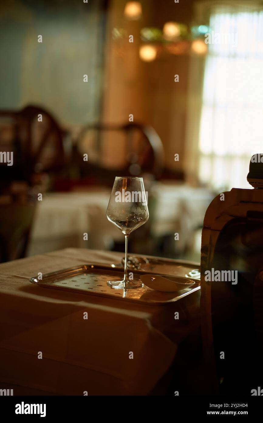A wine glass casts a soft reflection on an elegant dining table set in a restaurant with a ...