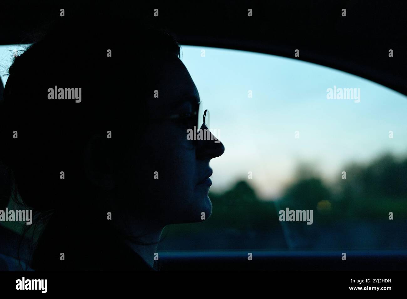 Silhouette of a woman in profile view looking forward through a car window during twilight Stock ...